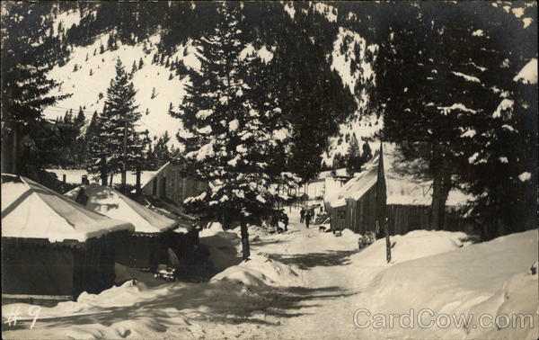 Small, Snow Covered Village Near Mountains Buildings Postcard
